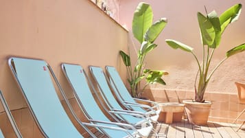 Fileira de cadeiras de descanso azuis e uma pequena mesa em um deck de madeira com plantas em vasos.