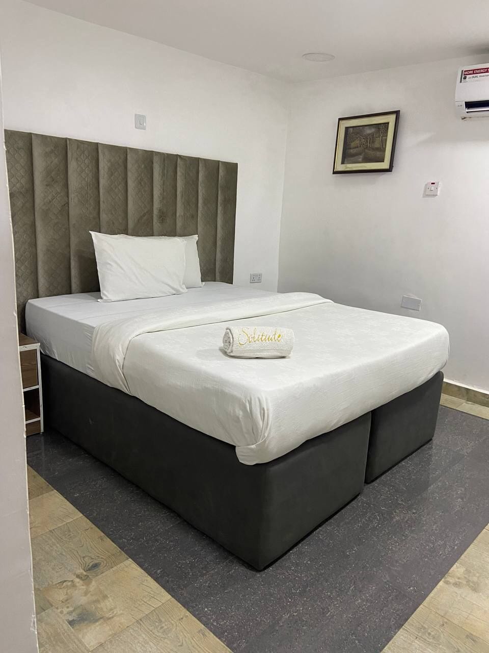 Cama bem arrumada com edredom branco e toalha com a palavra 'Solitude'.