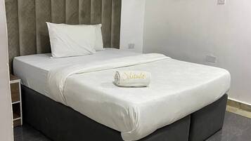 Cama bem arrumada com edredom branco e toalha com a palavra 'Solitude'.
