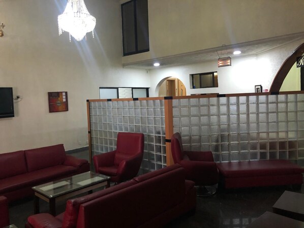 Um hall com assentos vermelhos, uma mesa de centro de vidro, um lustre e um divisório com padrão de grade.