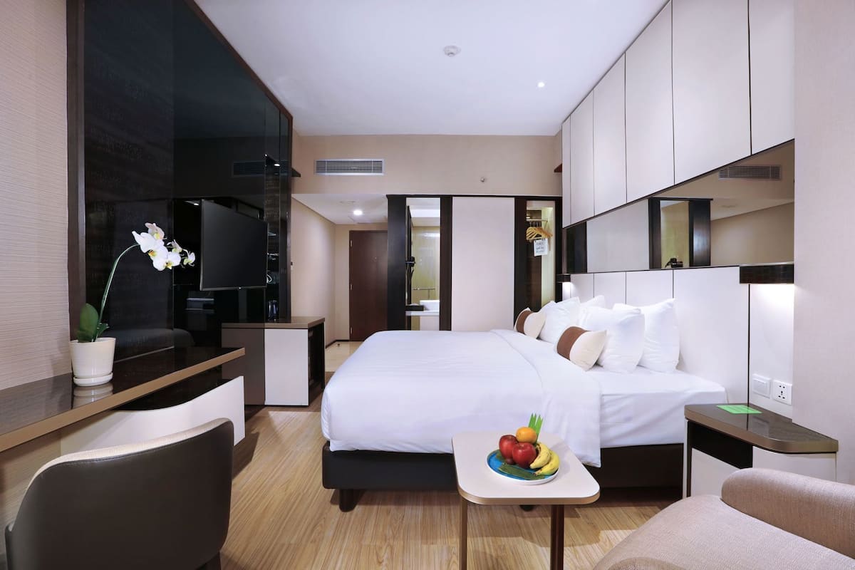 Quarto de hotel com cama, mesa de cabeceira, cadeira, escrivaninha, televisão e um vaso de planta.