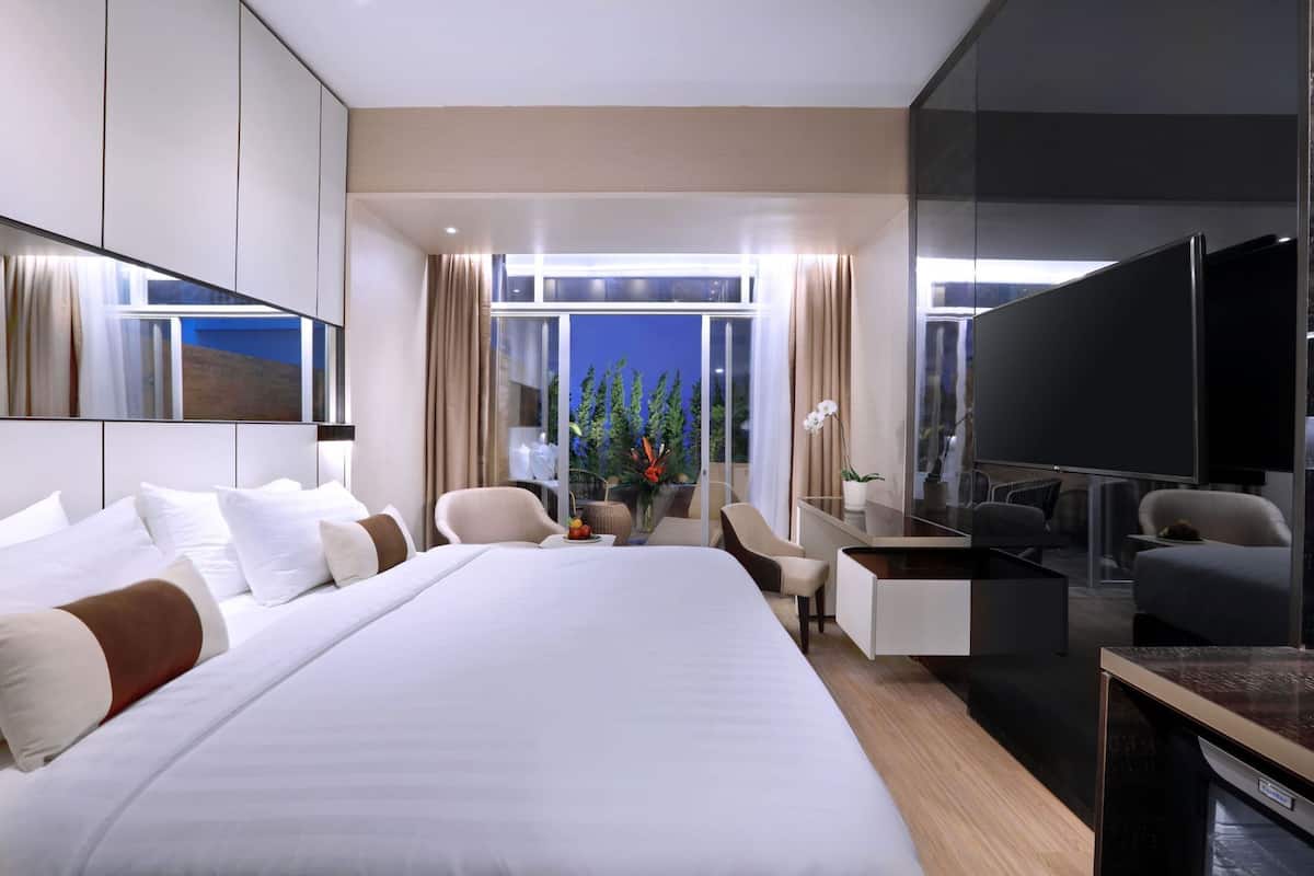 Quarto de hotel moderno com uma cama grande, uma escrivaninha, uma televisão e vista para a cidade.