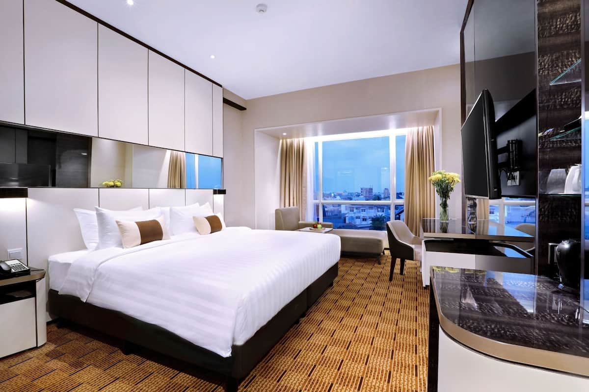 Quarto de hotel moderno com uma cama grande, uma escrivaninha, uma cadeira e vista para a cidade.