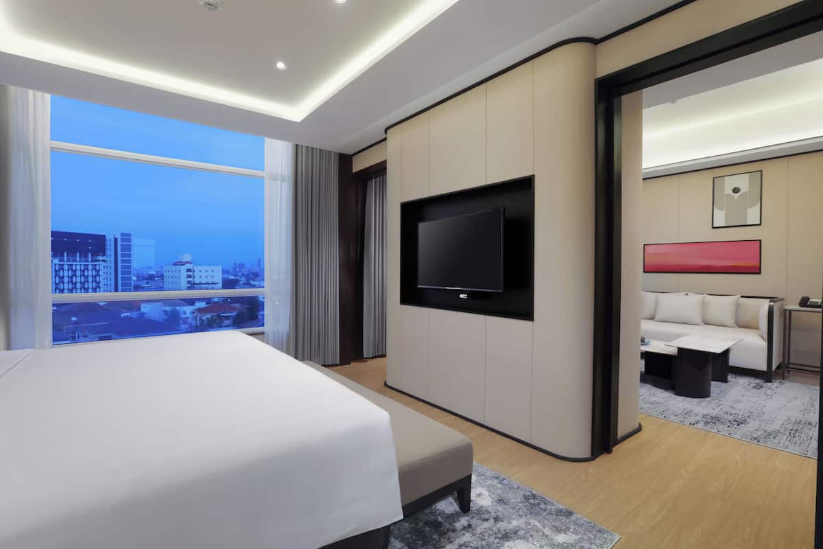 Quarto de hotel moderno com uma cama grande, televisão de tela plana na parede, um sofá e uma mesinha.
