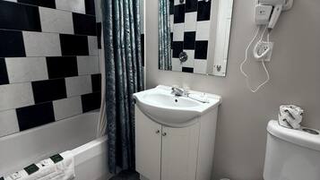Um banheiro com parede de azulejos quadriculada em preto e branco, chuveiro com cortina, pia com espelho acima e vaso sanitário.