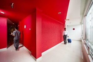 Corredor com paredes vermelhas e chão branco, que leva a uma porta de vidro.