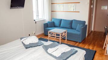 Quarto de hotel com cama, sofá azul, mesinha de madeira e televisão na parede.