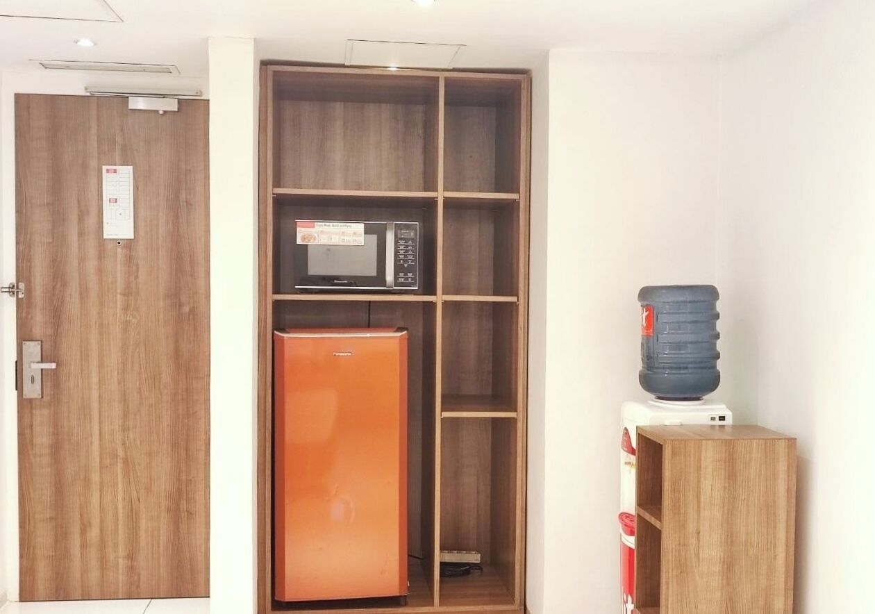 Quarto compacto com guarda-roupa de madeira, pequeno frigorífico, micro-ondas e dispensador de água.