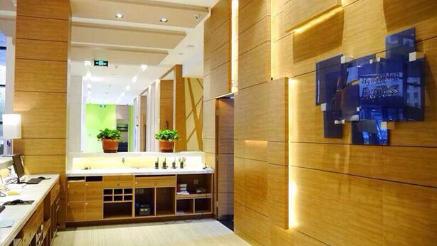 Um hall de hotel moderno com um balcão de recepção de madeira, um espelho grande e um painel de exibição digital.
