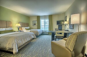 Quarto de hotel com duas camas, uma escrivaninha, uma cadeira, uma televisão e uma janela com cortinas.