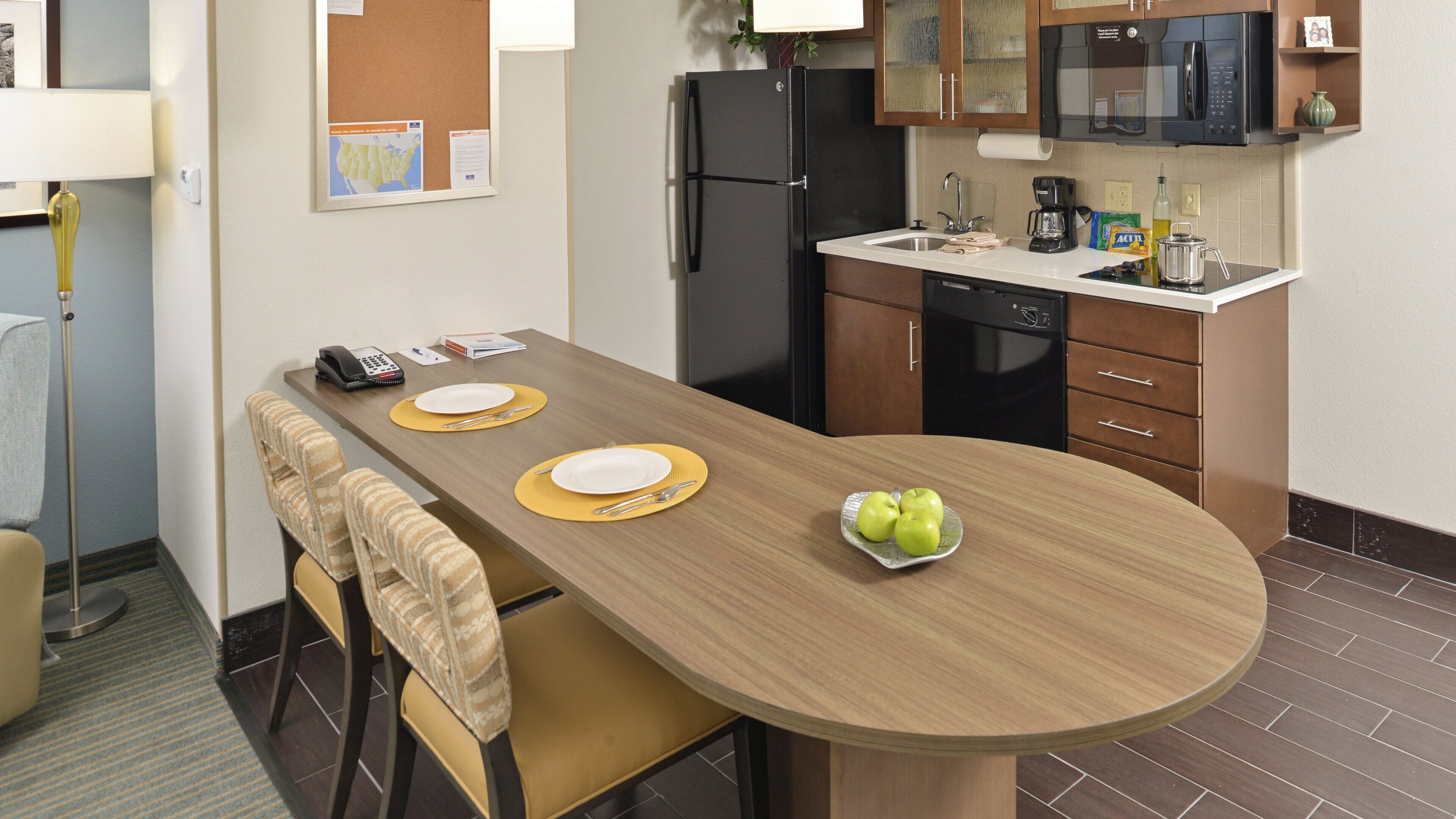 Quarto de hotel com uma mesa de jantar posta para dois, geladeira, micro-ondas e cafeteira.