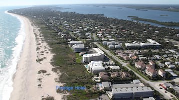 Vista aérea de uma área costeira com praia, um hotel chamado Prestige Hotel e edifícios residenciais ao redor.