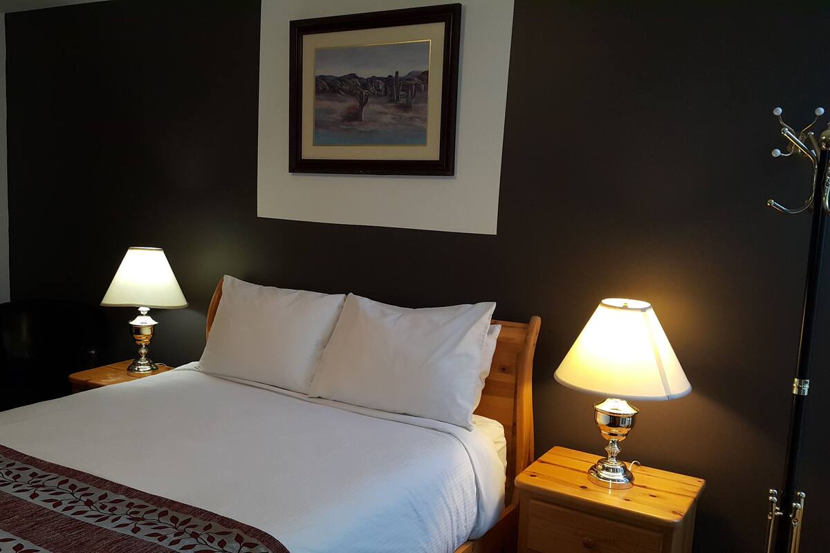 Quarto de hotel com cama, duas luminárias de cabeceira, um quadro na parede e uma janela com cortinas.