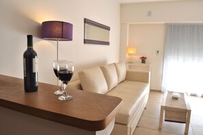 Uma sala de estar moderna com um sofá, uma mesa de centro, um abajur, uma garrafa de vinho e duas taças de vinho sobre uma mesinha de madeira.