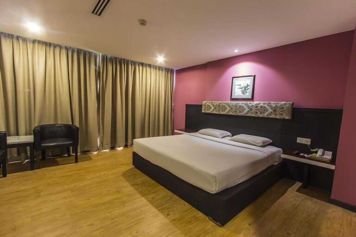 Quarto de hotel com uma cama, uma escrivaninha, uma cadeira e uma mesinha de cabeceira.