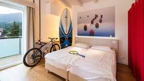 Quarto com uma cama, uma bicicleta e uma prancha de surf encostadas na parede.