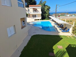 Uma piscina com espreguiçadeiras, um edifício com varandas e vista para o mar.