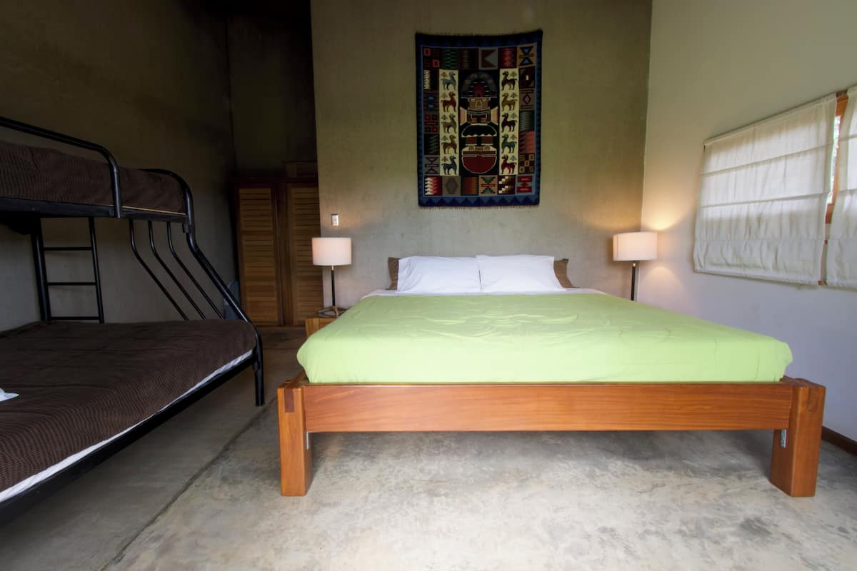 Quarto com uma cama de solteiro, uma cama individual com colchão verde, duas luminárias de cabeceira e uma tapeçaria decorativa na parede.