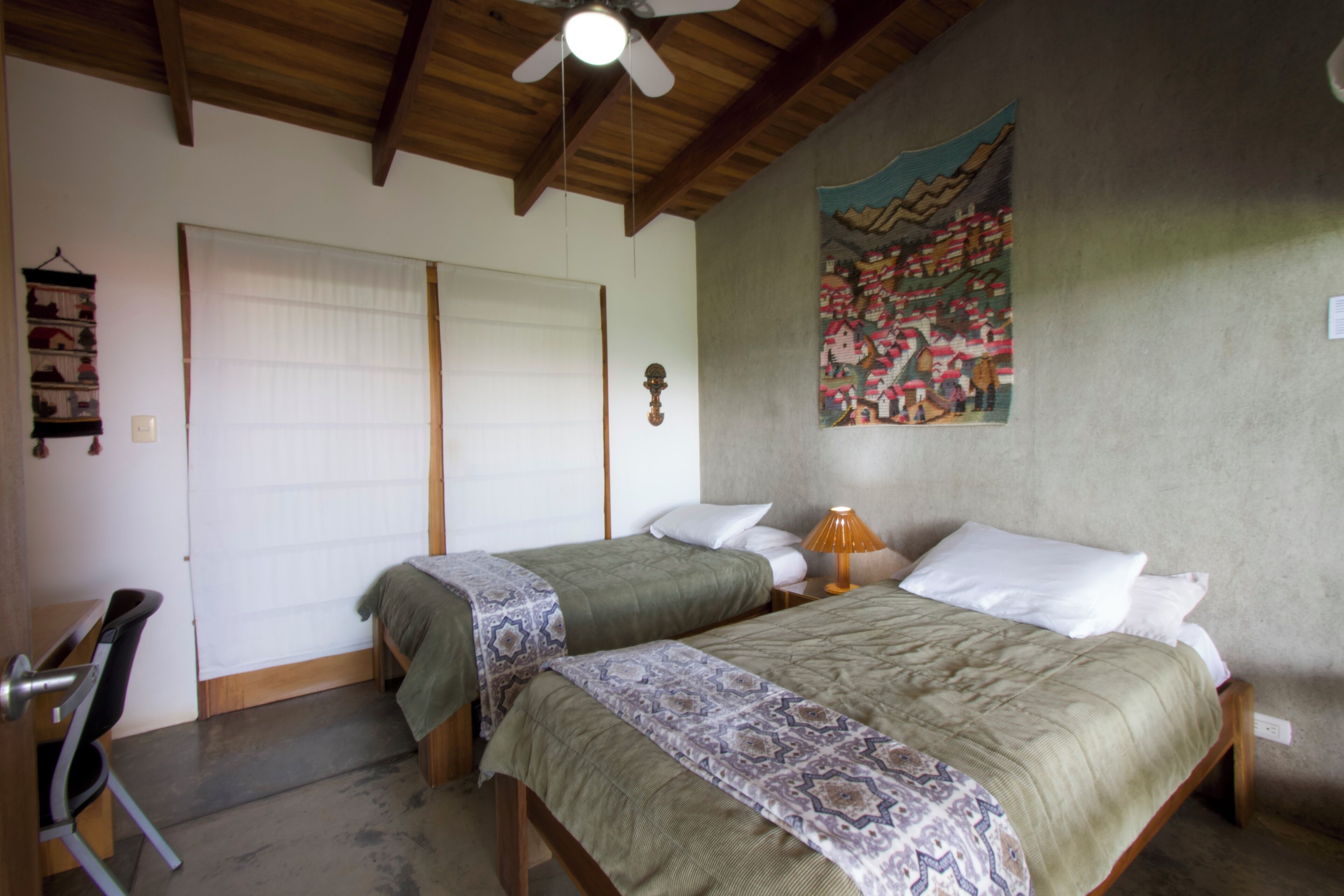 Quarto com duas camas, uma escrivaninha e um ventilador de teto.