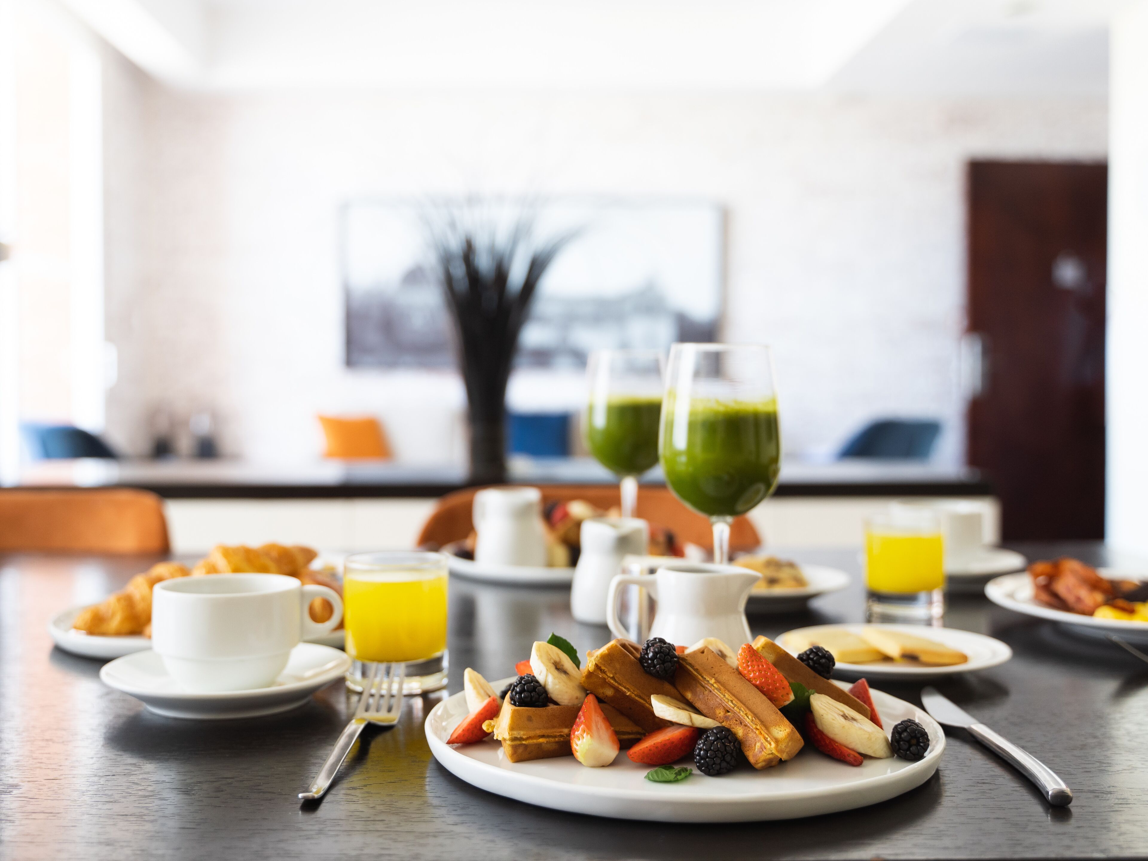 Disposição para o café da manhã com pratos de comida, uma xícara de café e copos de suco.
