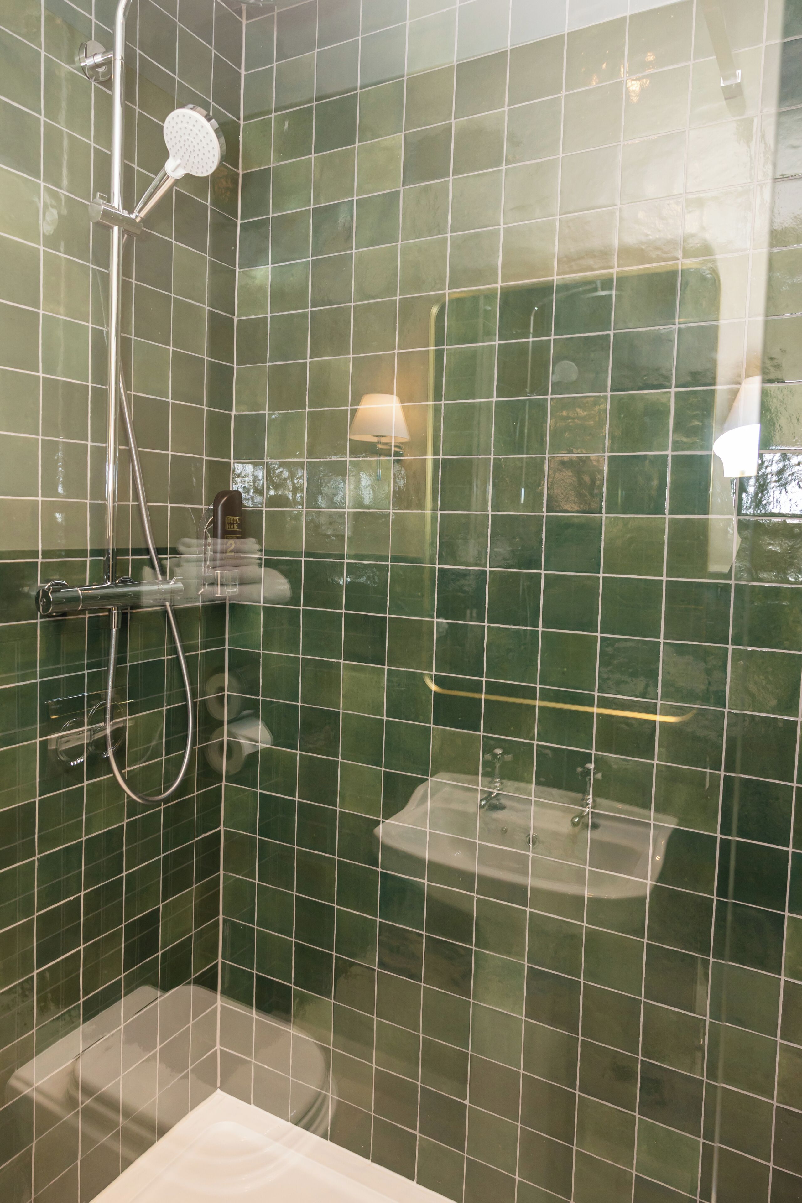Casa de banho com paredes em azulejo verde, chuveiro e lavatório.