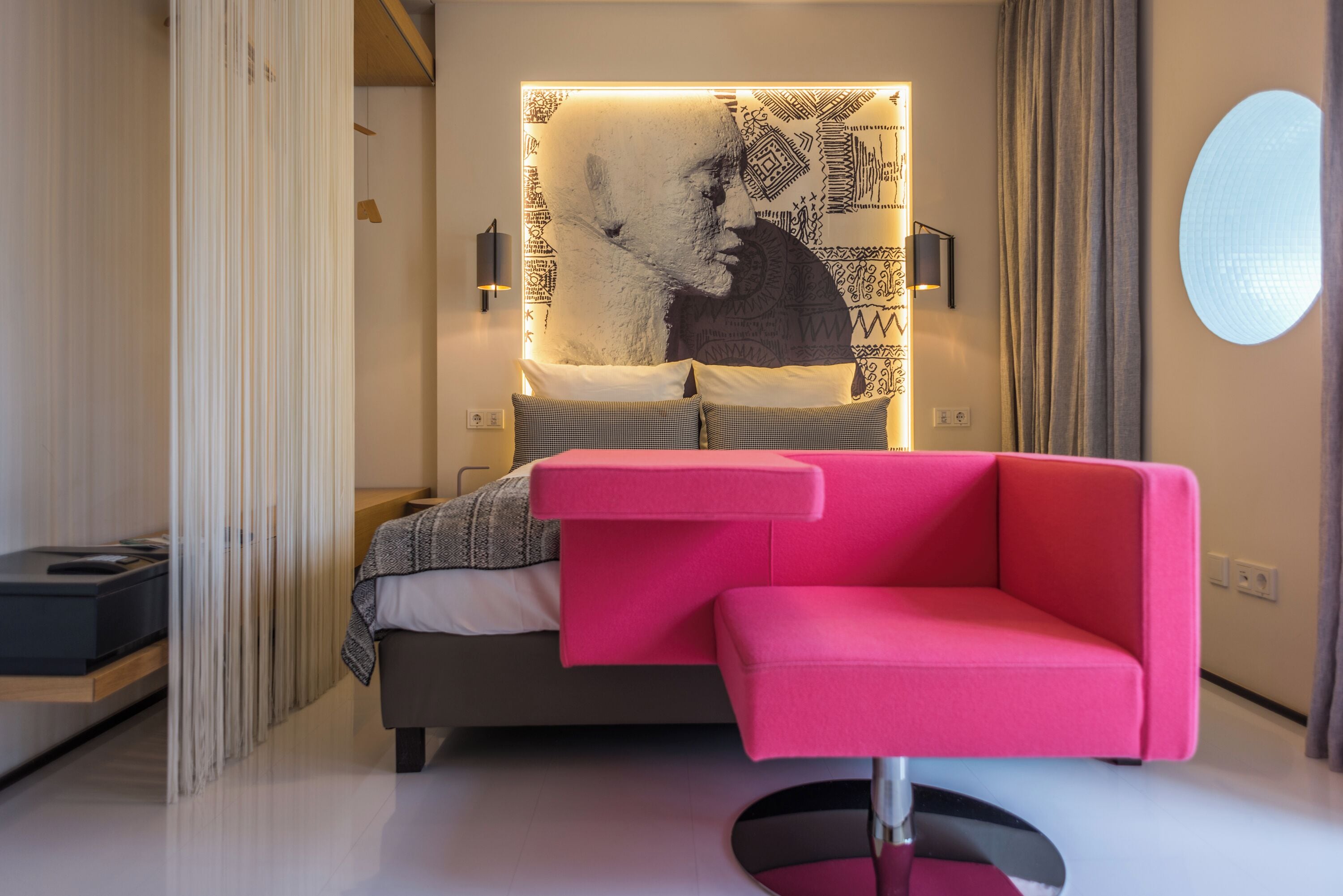 Quarto moderno com cama, uma cadeira rosa e uma parede com uma grande obra de arte.