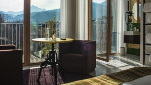Quarto de hotel com uma cama grande, varanda com vista para montanhas, mesa de jantar com um vaso e um candelabro.
