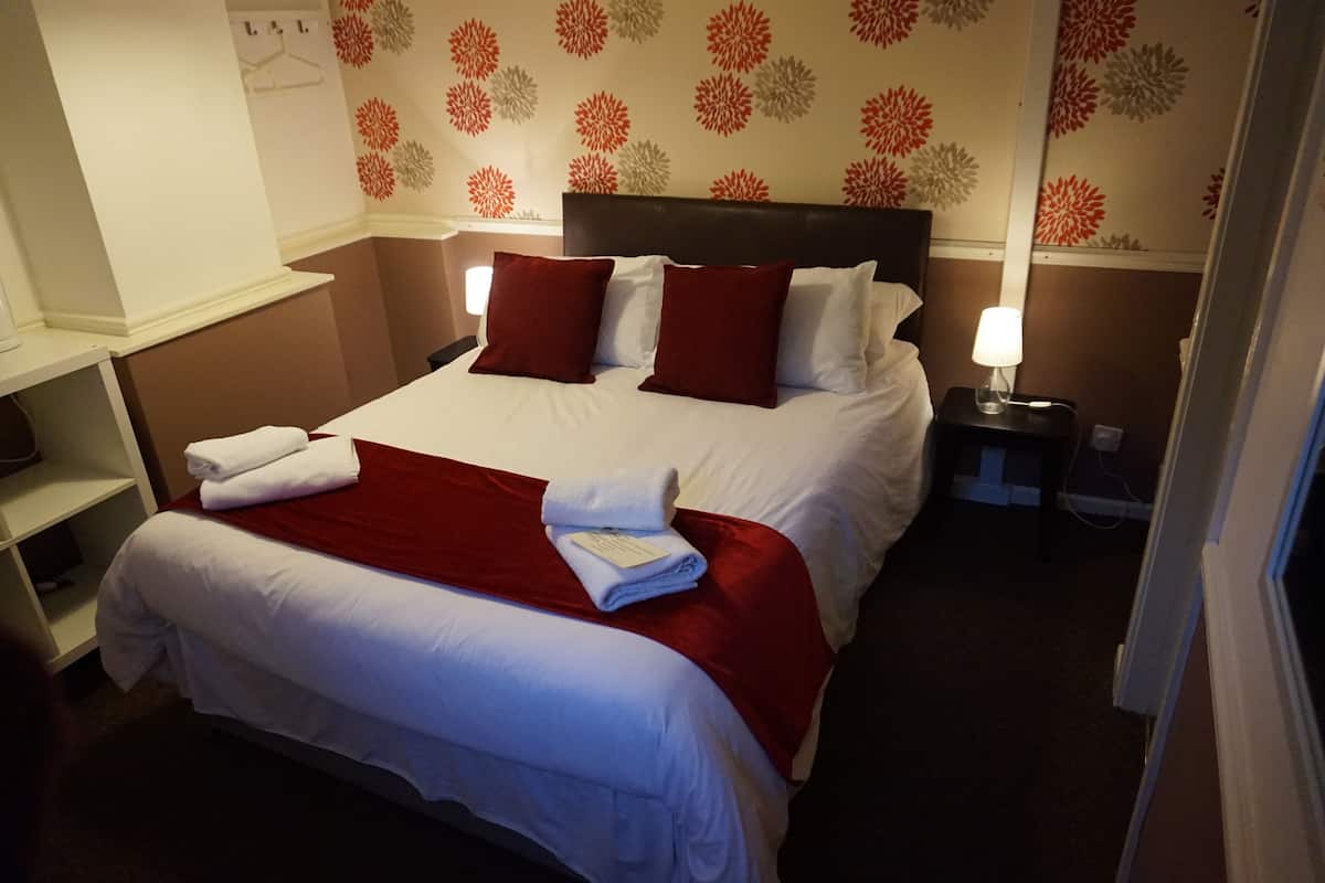 Cama bem arrumada com roupa de cama vermelha e branca, duas luminárias de cabeceira e um cobertor vermelho.