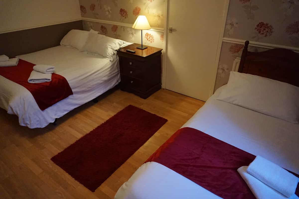 Quarto de hotel com duas camas, uma mesa de cabeceira com abajur e um tapete vermelho.