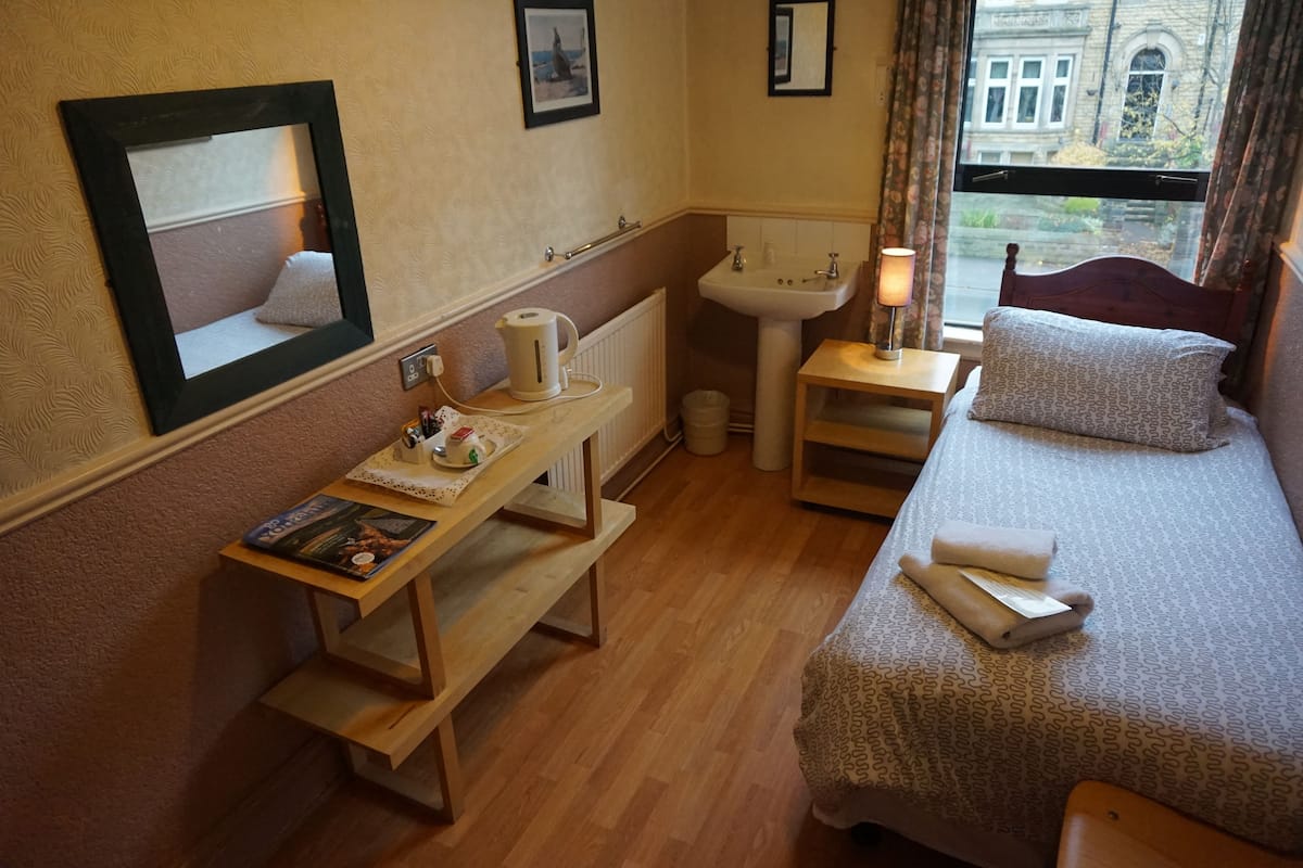 Quarto de hotel com cama, mesa de cabeceira, espelho e janela com vista para edifícios.
