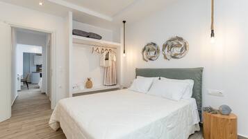 Um quarto com cama, guarda-roupa, mesa de cabeceira redonda de madeira e luminária fixada na parede.