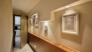 Um corredor com obras de arte emolduradas nas paredes, um banco de madeira e uma porta que dá para uma cozinha.