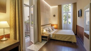 Quarto de hotel com cama, mesa de cabeceira, luminária e janela com cortinas.