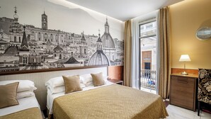Quarto de hotel com um grande mural da paisagem urbana, duas camas com cabeceiras iguais, uma escrivaninha com abajur e vista para a cidade por uma ampla janela.