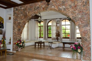Quarto com paredes de pedra, um banco, uma mesa e uma janela com cortinas.