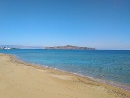 Uma praia com águas azul-claras e uma ilha rochosa ao longe.