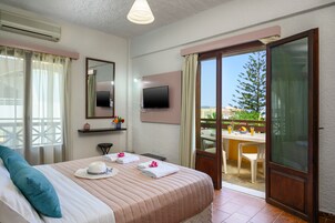 Quarto de hotel com cama, televisão, varanda com mesa e cadeiras, e vista para o exterior.