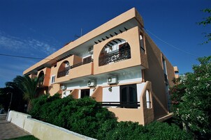 Um edifício de dois andares com telhado plano, várias varandas e aparelhos de ar condicionado.