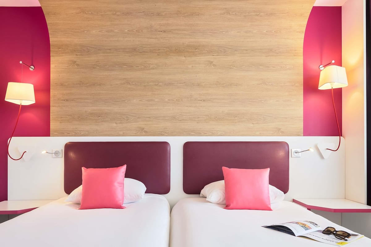 Quarto de hotel com duas camas, cada uma com cabeceira, teto de madeira e luminárias fixadas na parede.