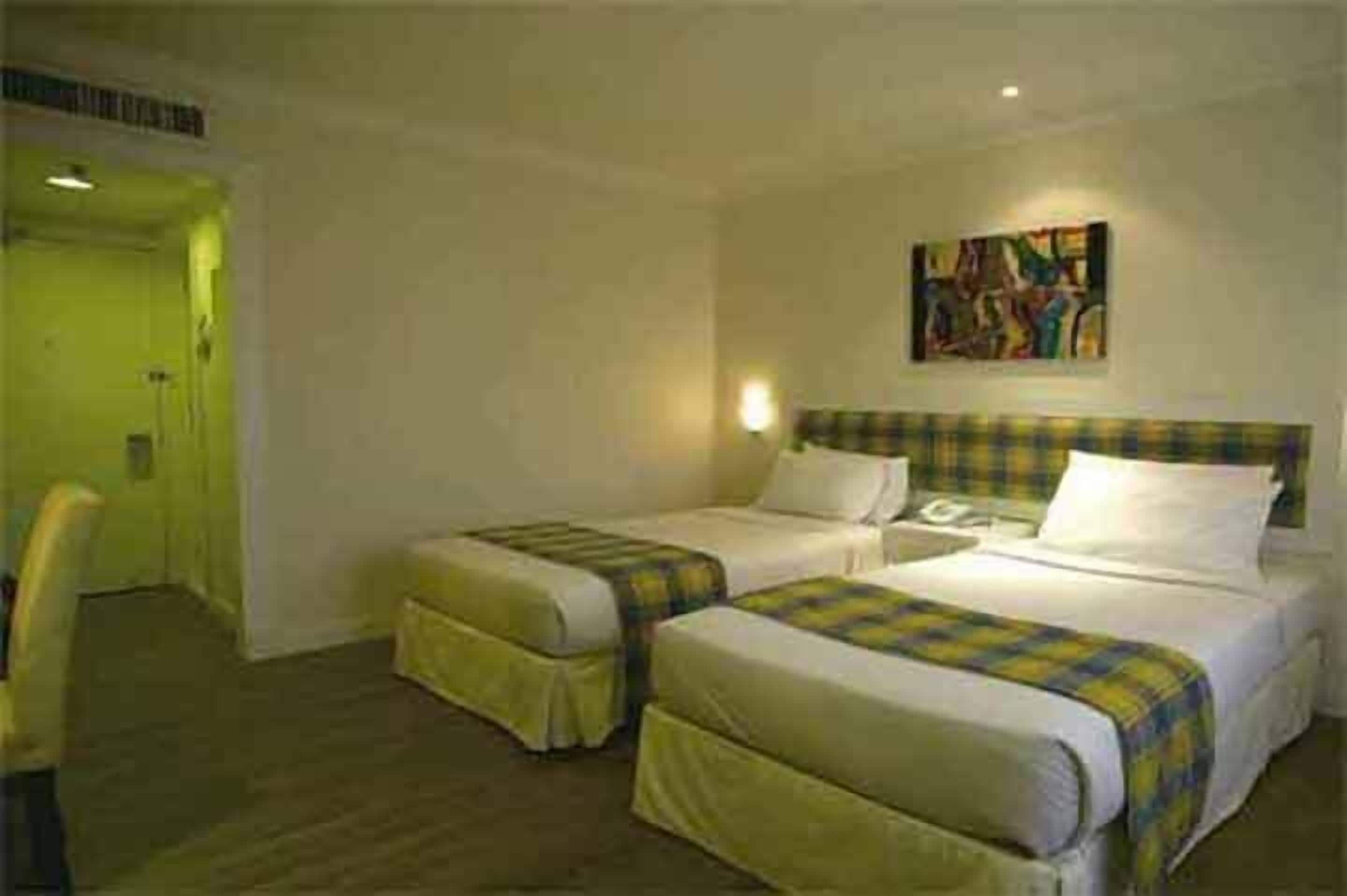 Quarto de hotel com duas camas, um quadro na parede e corredor iluminado em verde.
