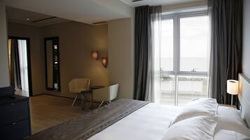 Quarto de hotel com uma cama grande, uma escrivaninha, uma cadeira e vista para a cidade pela janela.