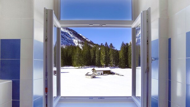 Casa de banho com vista para uma paisagem nevada e uma pequena cabana.