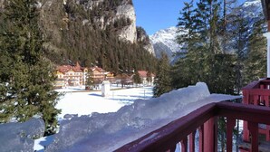 Paisagem coberta de neve com montanhas ao fundo, um deck de madeira e um prédio com telhados vermelhos.