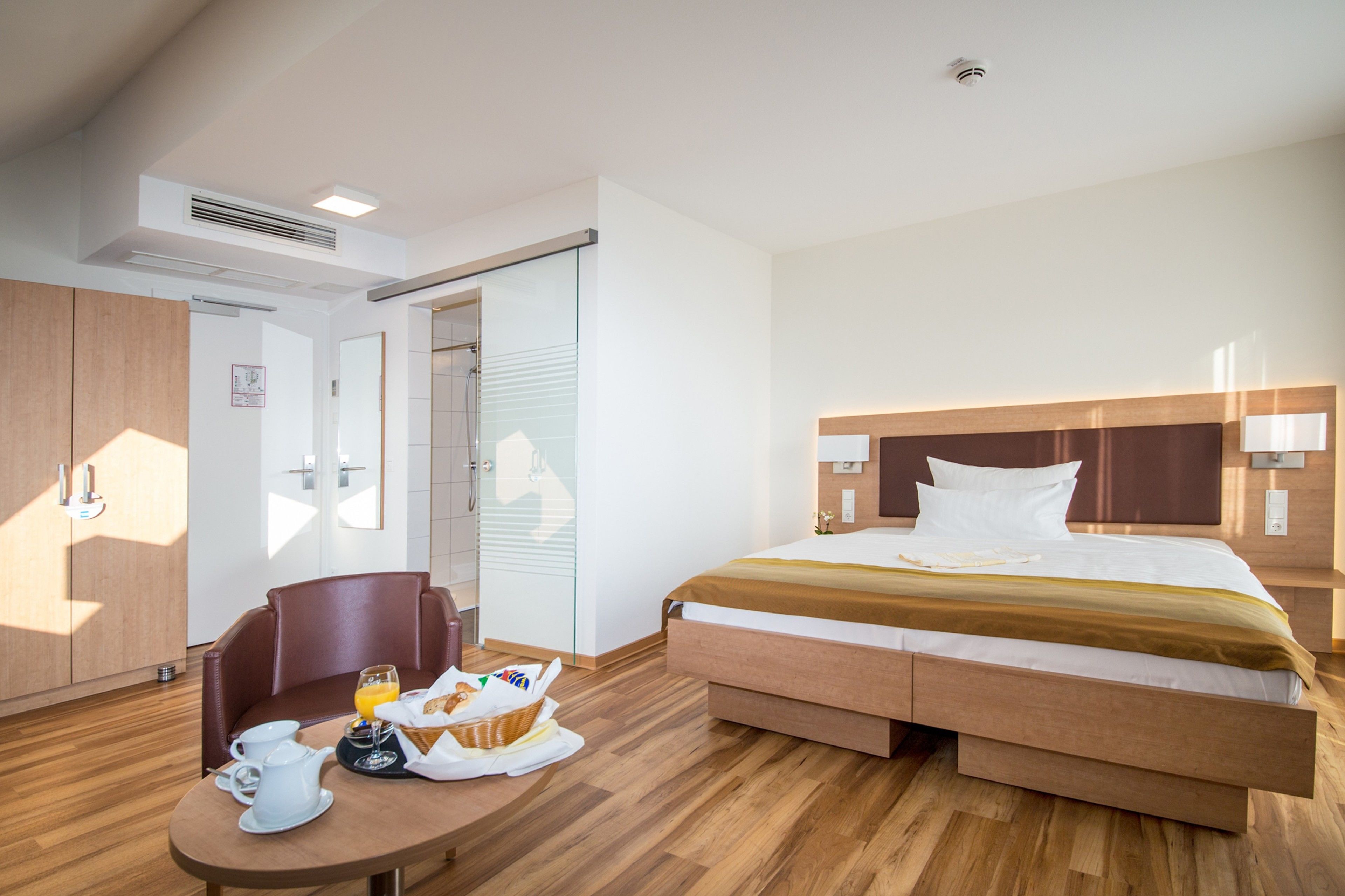 Quarto de hotel com cama, escrivaninha com cadeira, cafeteira e bandeja de café da manhã.