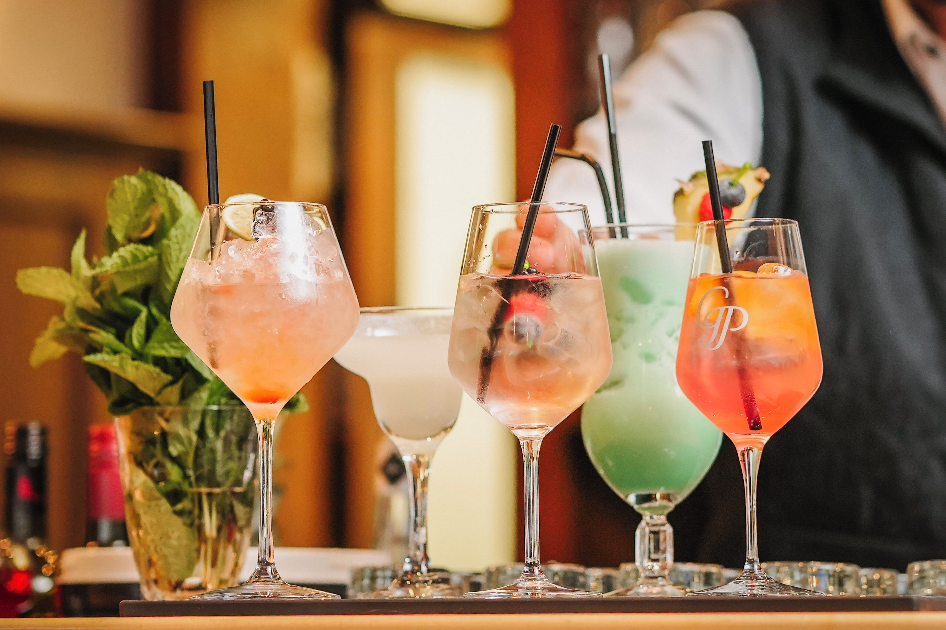 Um bar com quatro coquetéis diferentes em copos de martini, cada um com canudo.