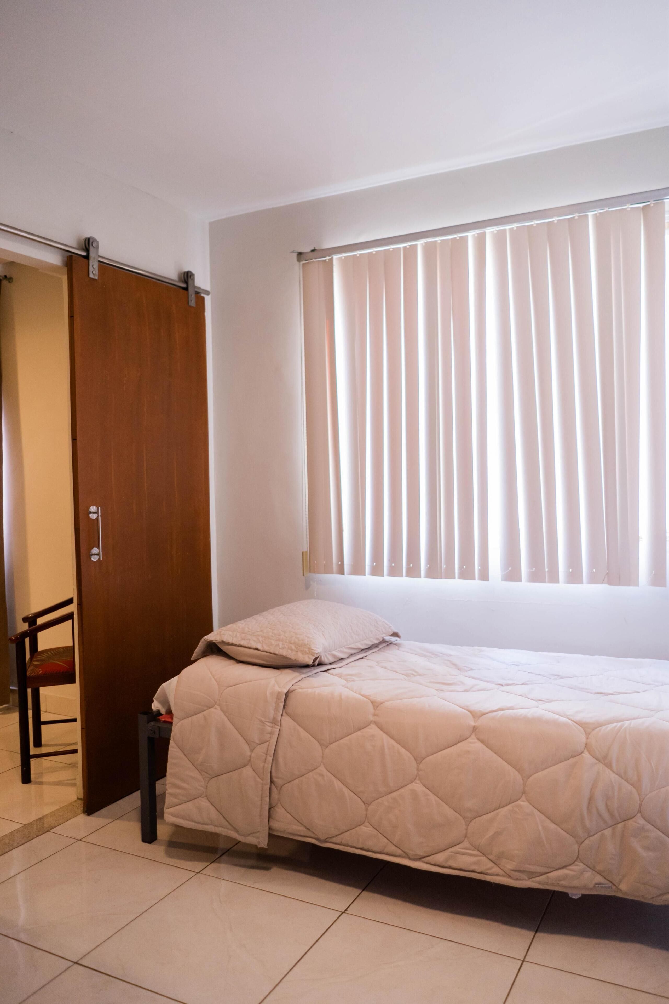 Um quarto com cama, porta de madeira e janela com cortinas.