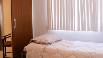 Um quarto com cama, porta de madeira e janela com cortinas.