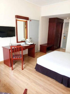 Quarto de hotel com uma cama, uma escrivaninha com cadeira, um espelho e um guarda-roupa.