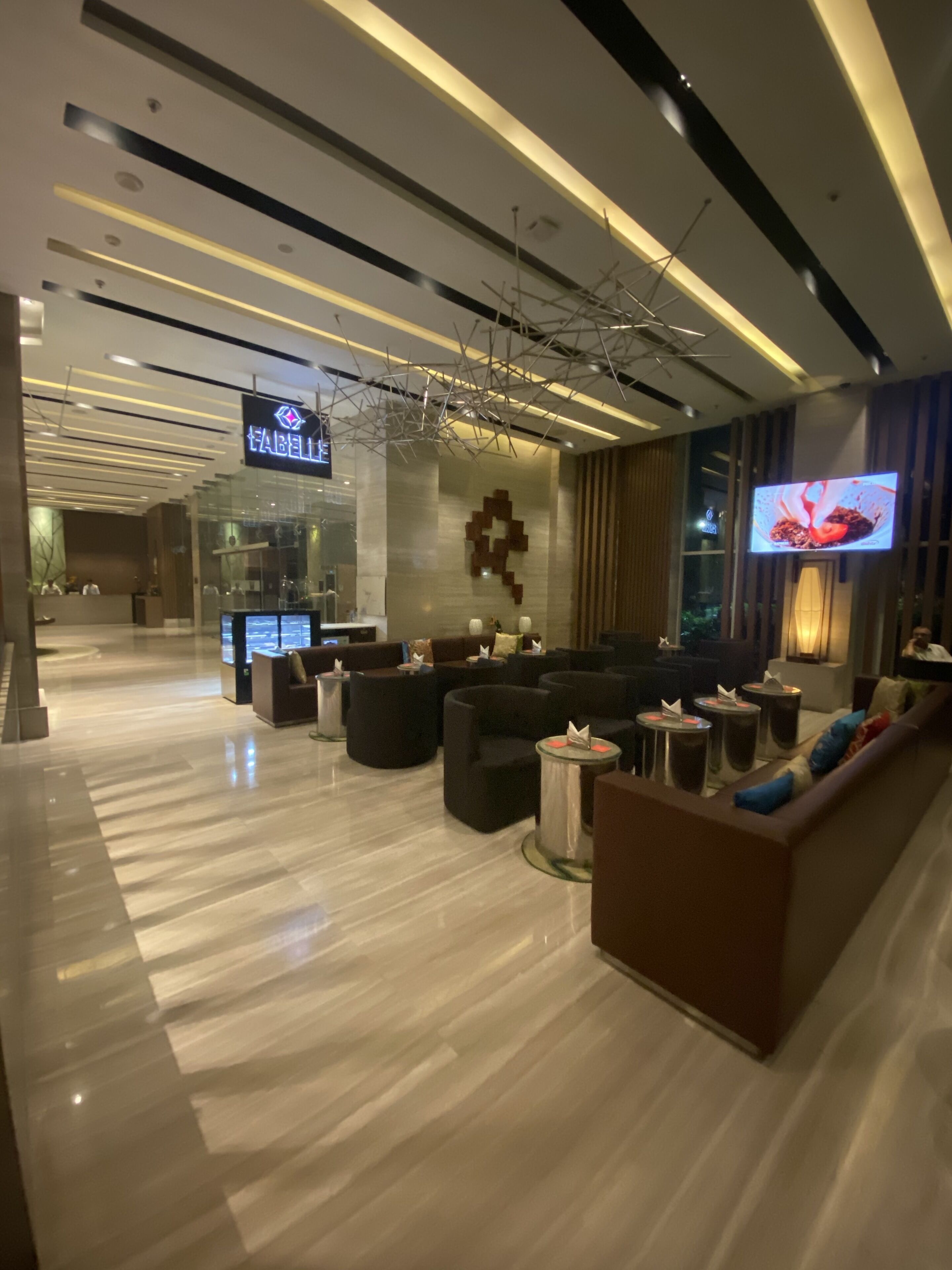 Um lobby moderno com uma mesa de recepção, área de estar e uma televisão exibindo um programa.
