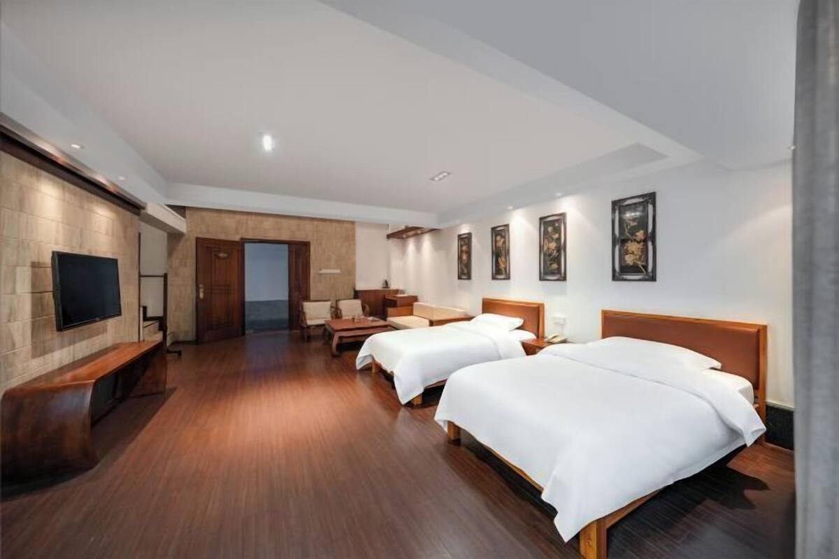 Quarto de hotel com duas camas, televisão, piso de madeira e obras de arte nas paredes.